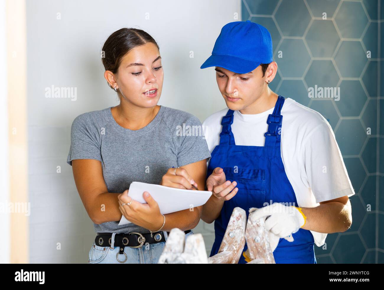 Girl homeowner discussing house renovation work plan with young builder ...