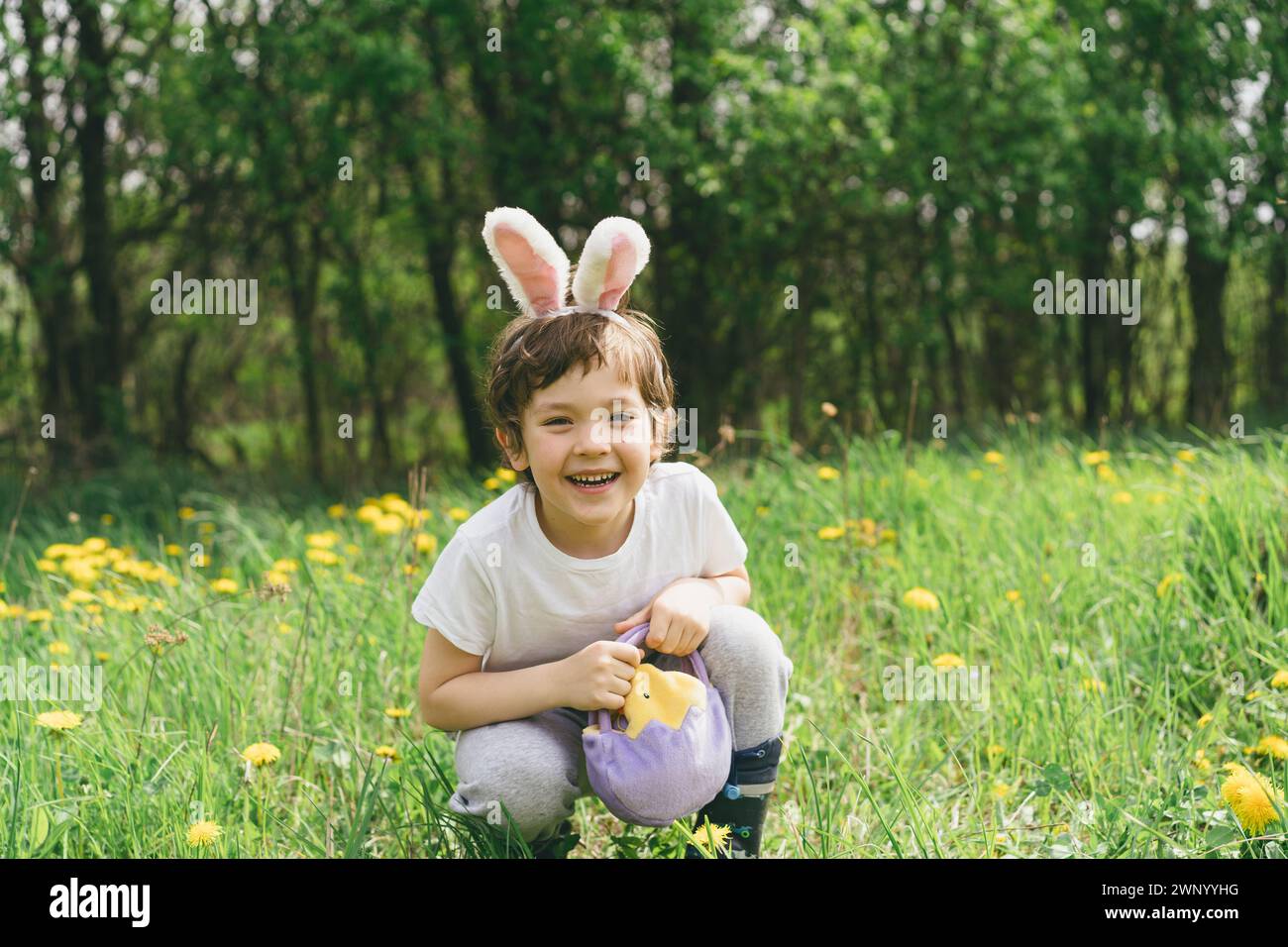 Boy with eggs basket and bunny ears on Easter egg hunt in sunny spring ...