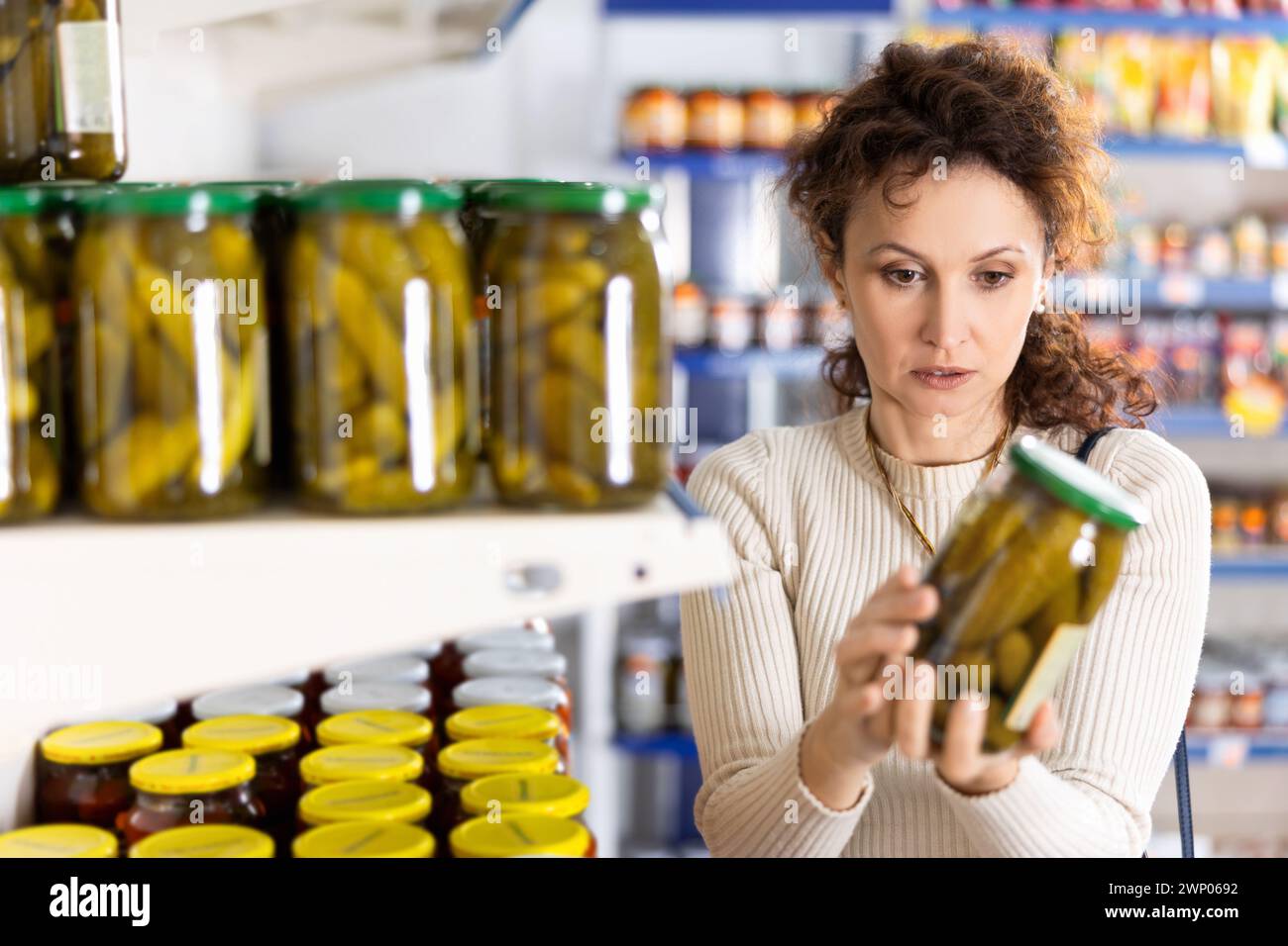 Adult female shopper in casual clothes chooses pickled cucumbers in ...