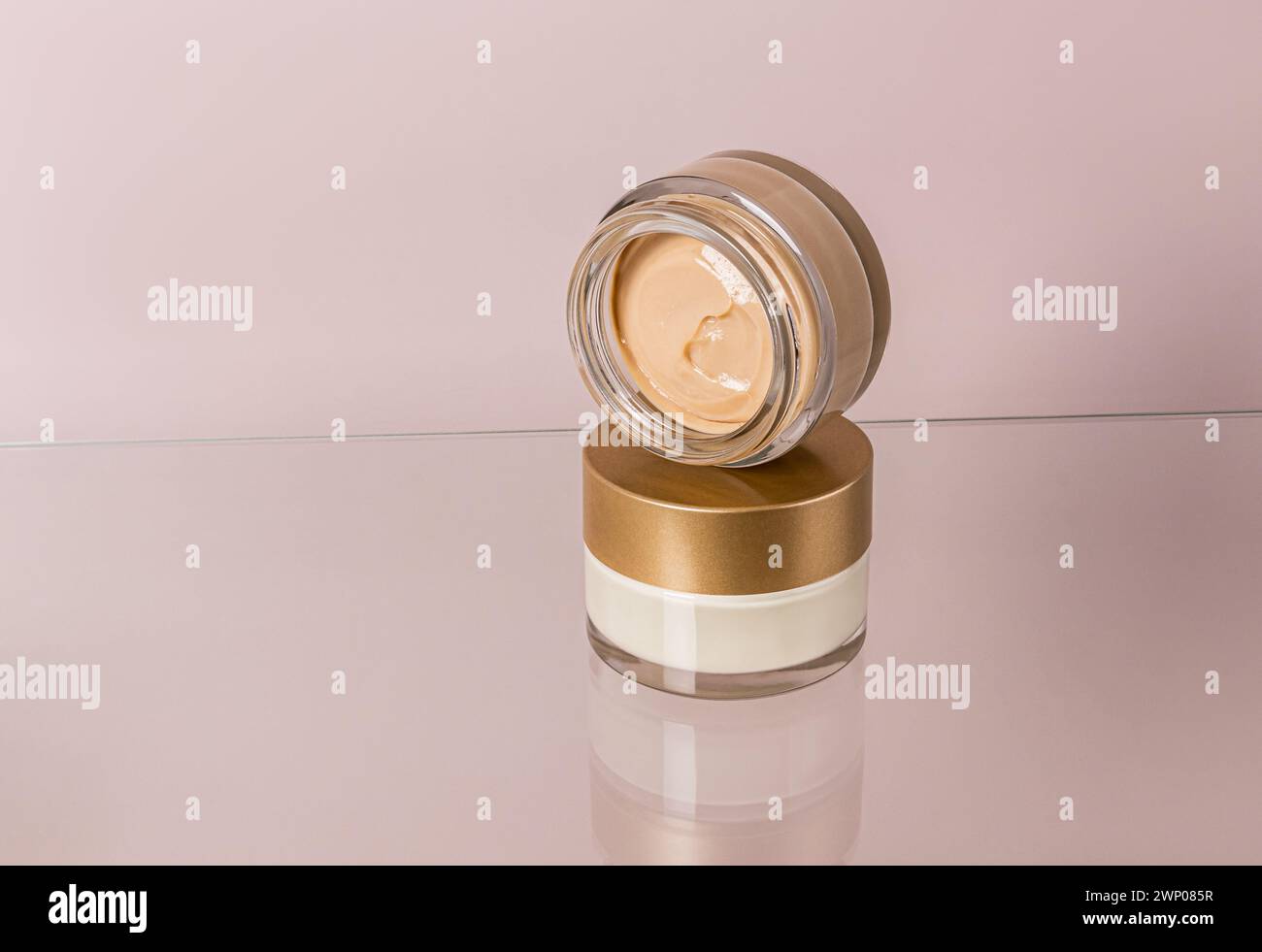 Two chic glass jars of cosmetic product on top of each other on glass ...