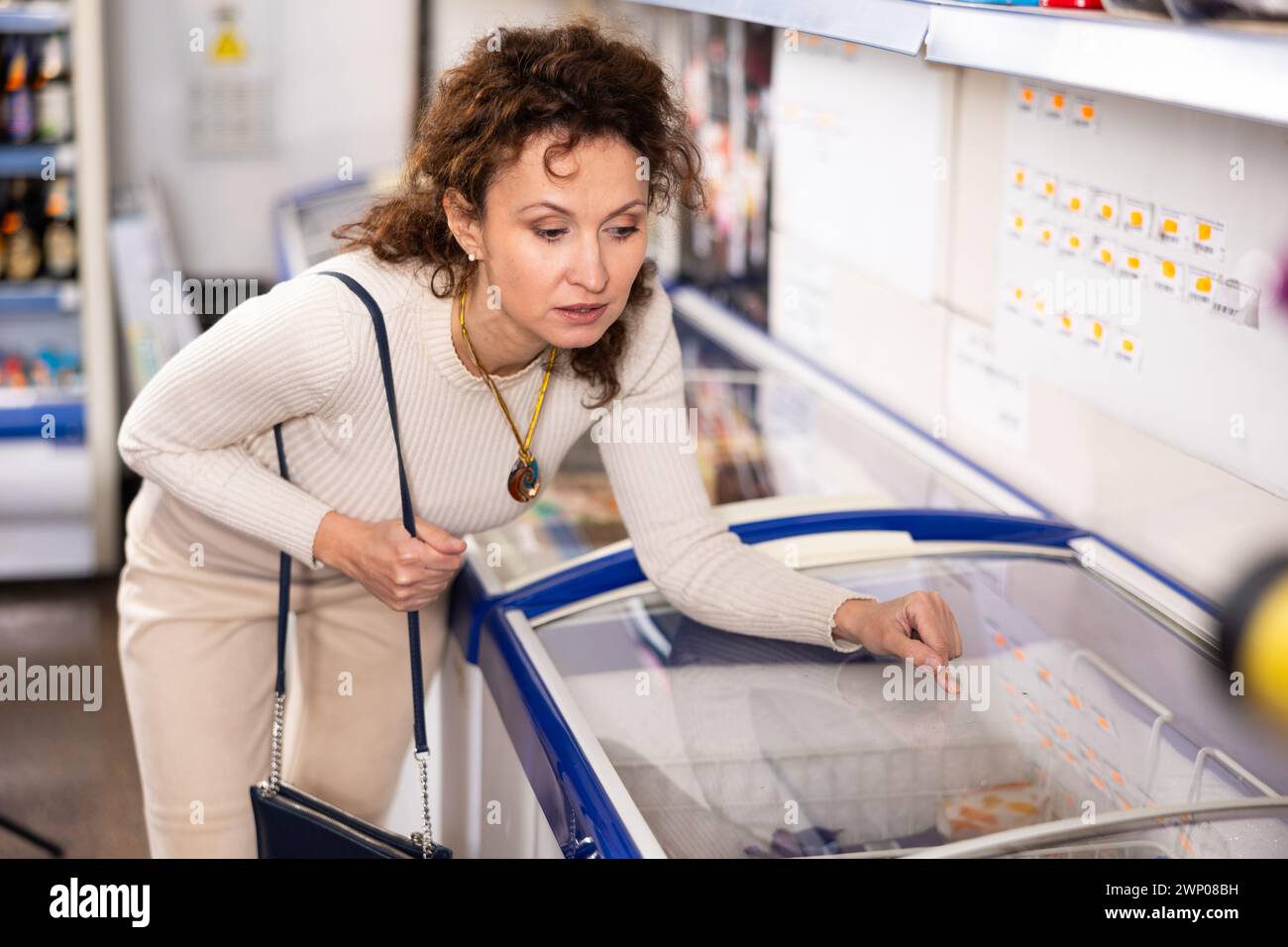 woman looks and chooses frozen food in refrigerator in grocery ...