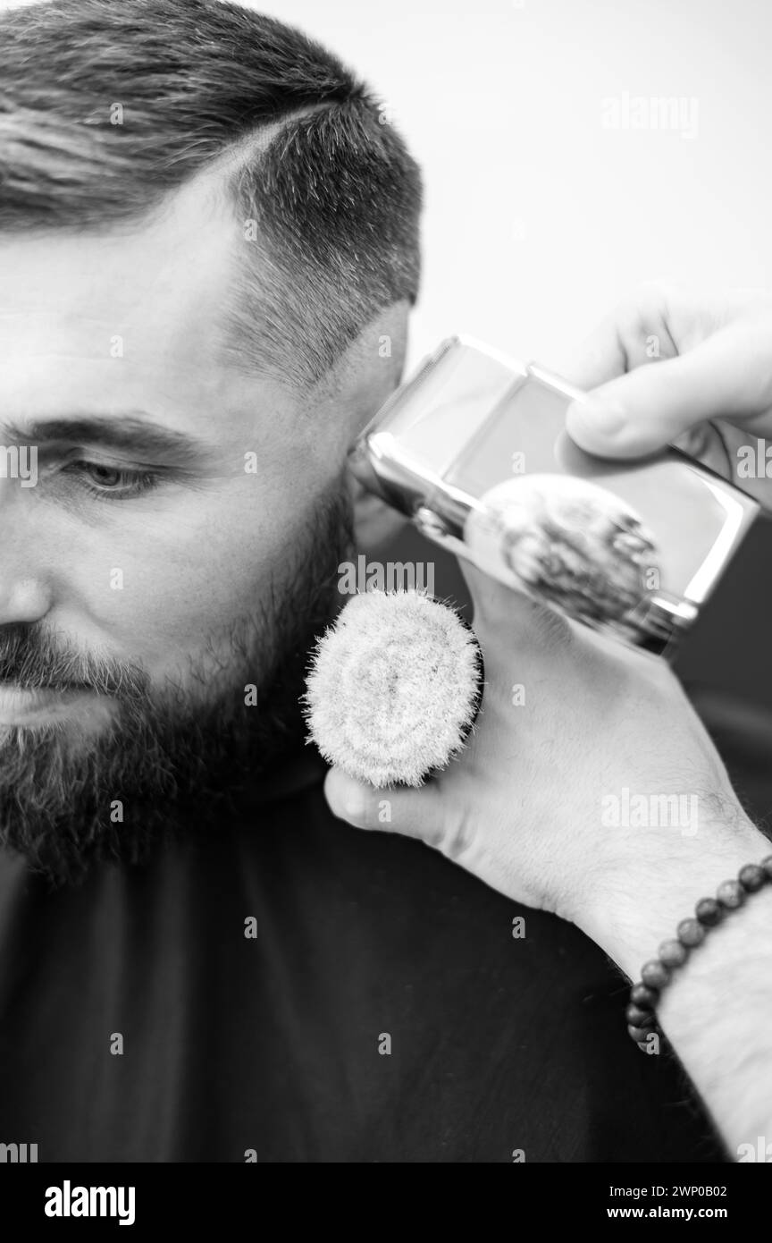 Barber shaves the temple with a cordless trimmer during a short haircut ...