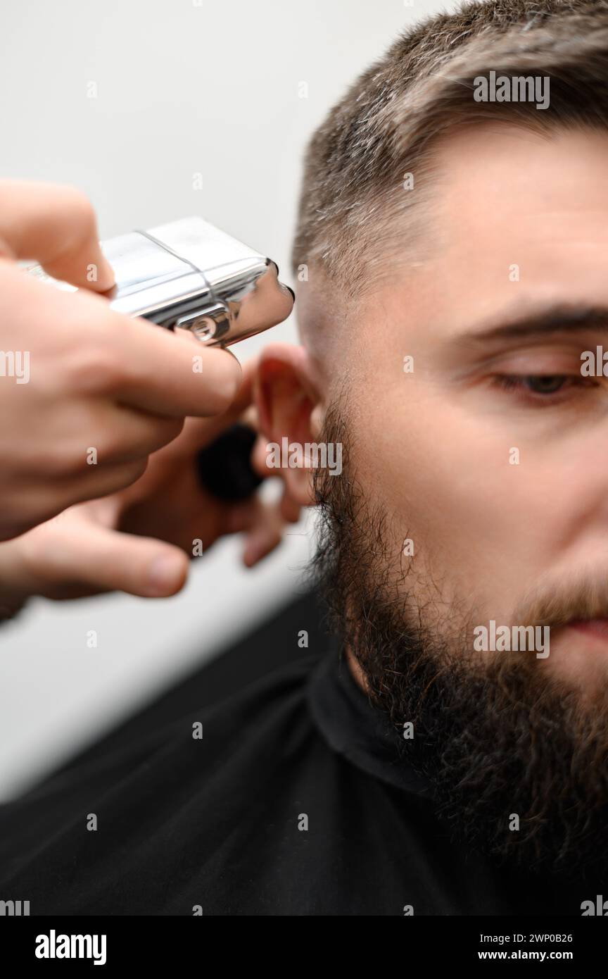 Barber shaves the temple with a cordless trimmer during a short haircut ...