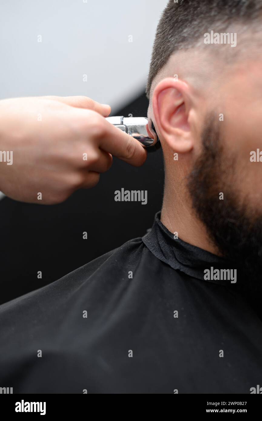 Barber shaves the temple with a cordless trimmer during a short haircut ...