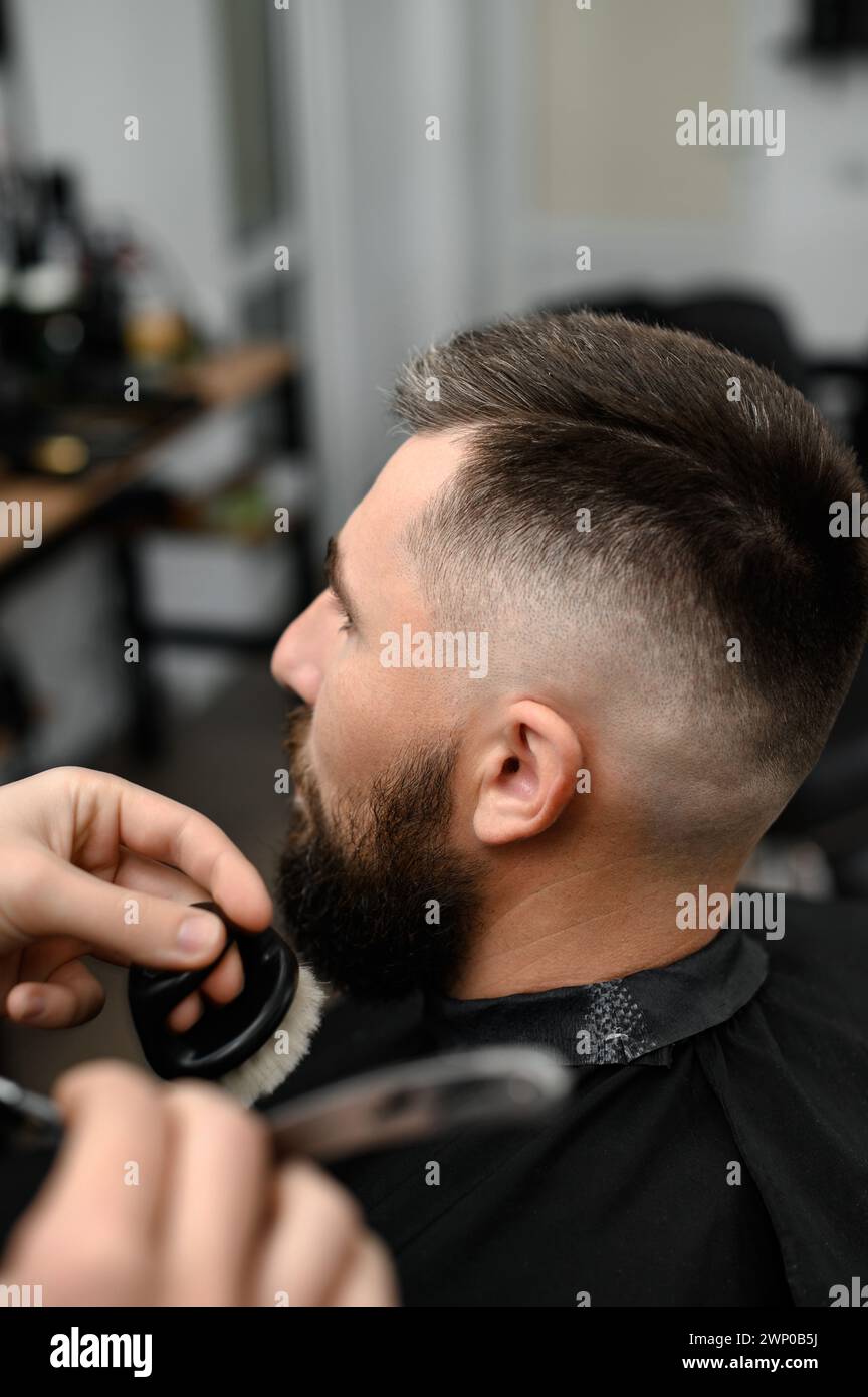 Barber sweeps hair with a brush while cutting a clients hair in a salon ...