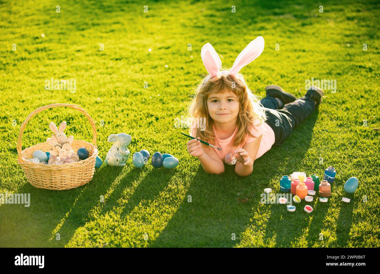 Child boy with easter eggs and bunny ears laying on grass. Easter kids ...
