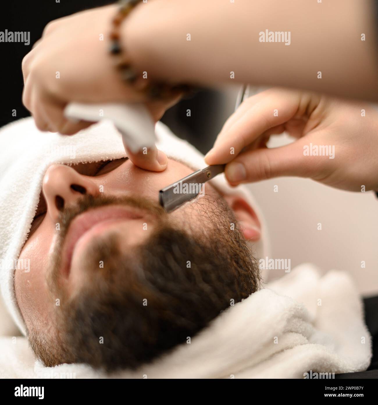 A barber shaves the cheek of a bearded customer with a dangerous razor ...