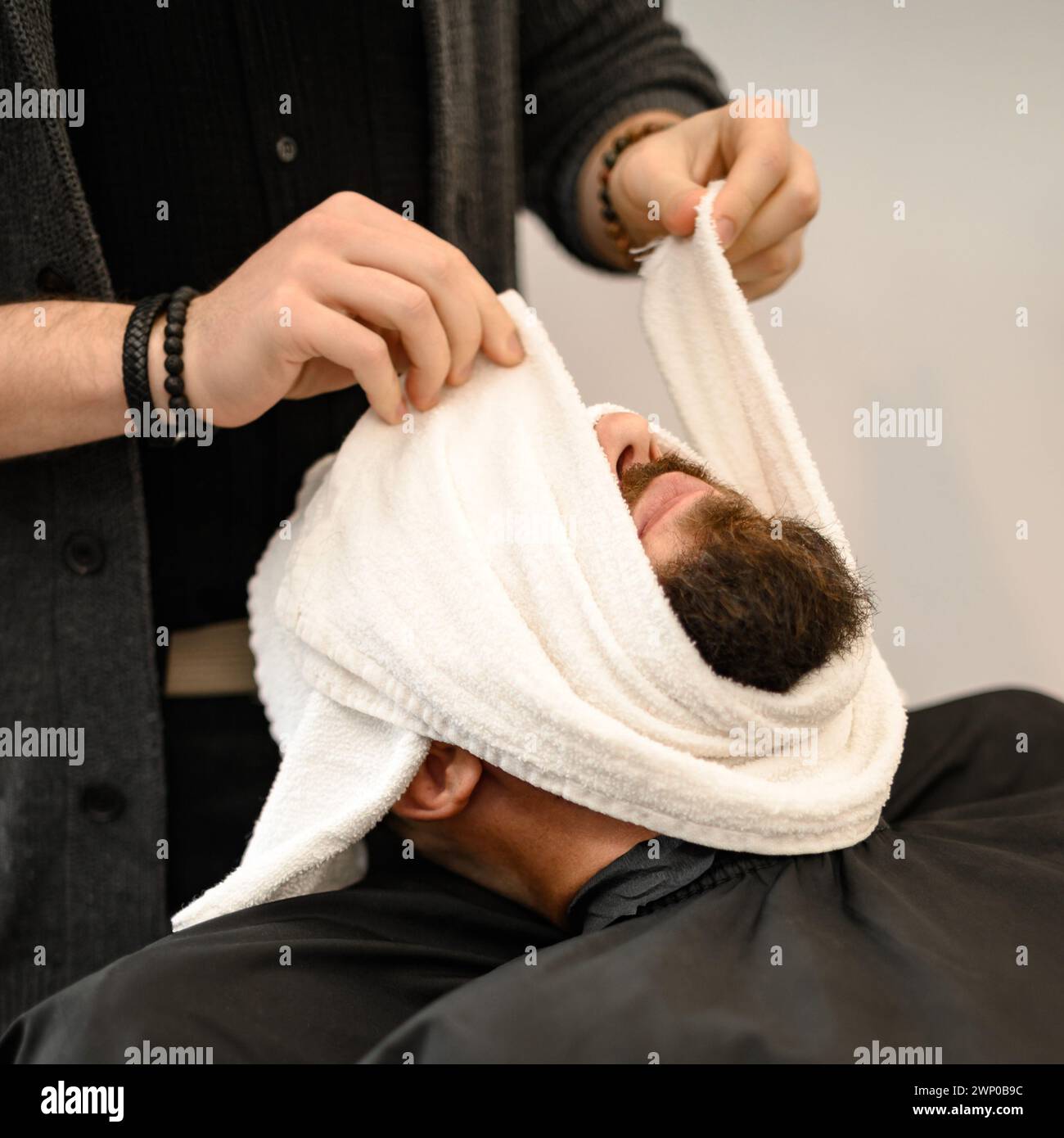 The barber covers the clients face with a hot wet towel to steam off ...