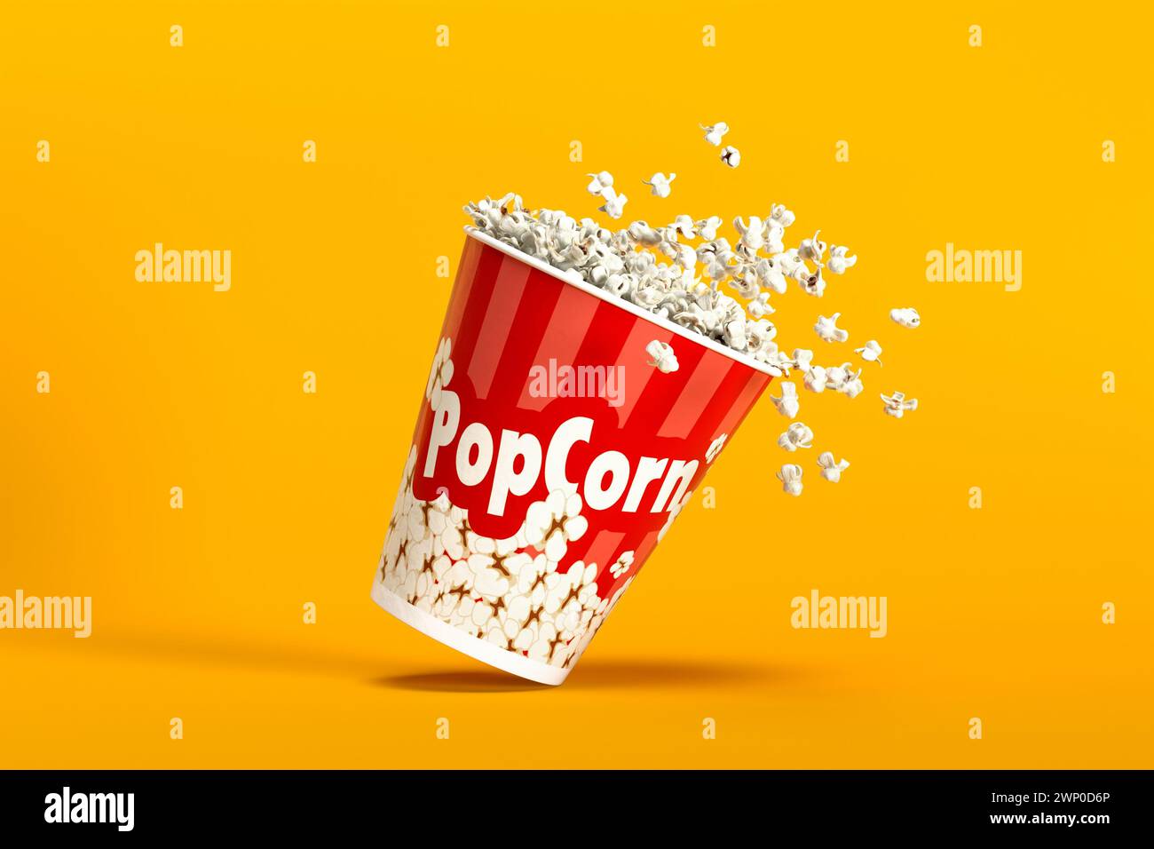 Big bucket of popcorn falling with spilling corns on yellow background ...