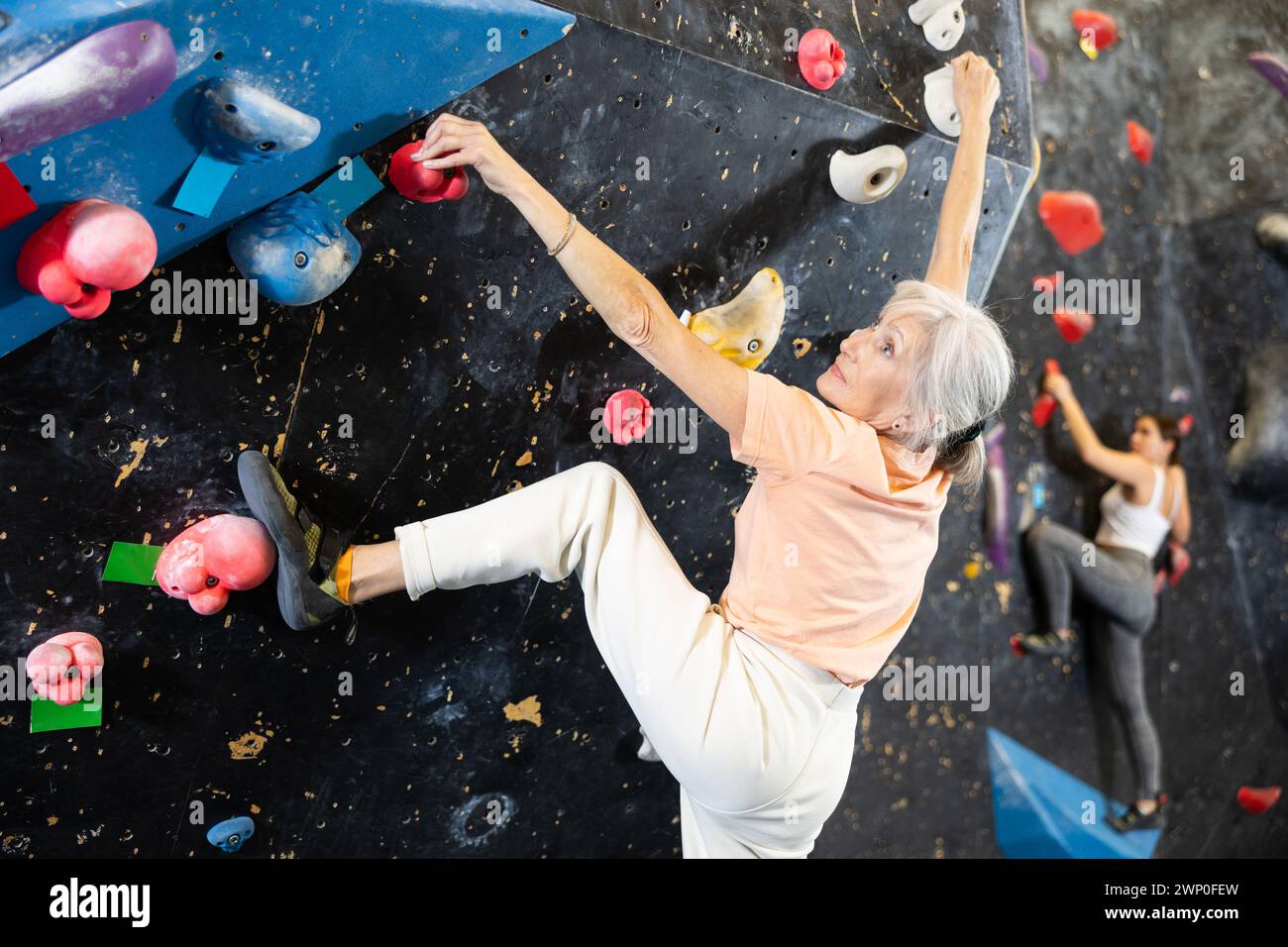 Mature female fitness climber training at bouldering gym.Woman rise up ...