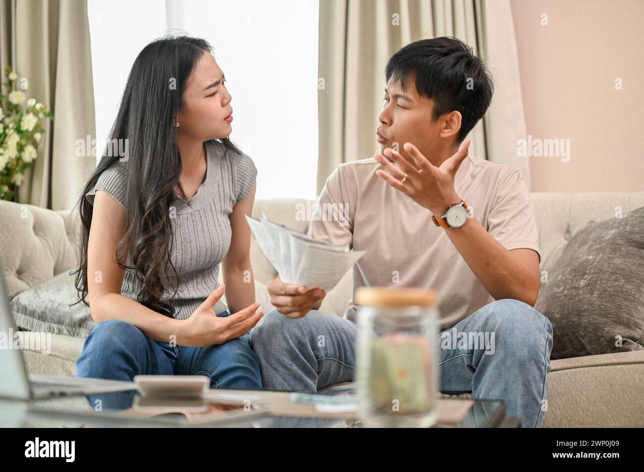 Unhappy, stressed Asian spouses are sitting on a couch, arguing about ...