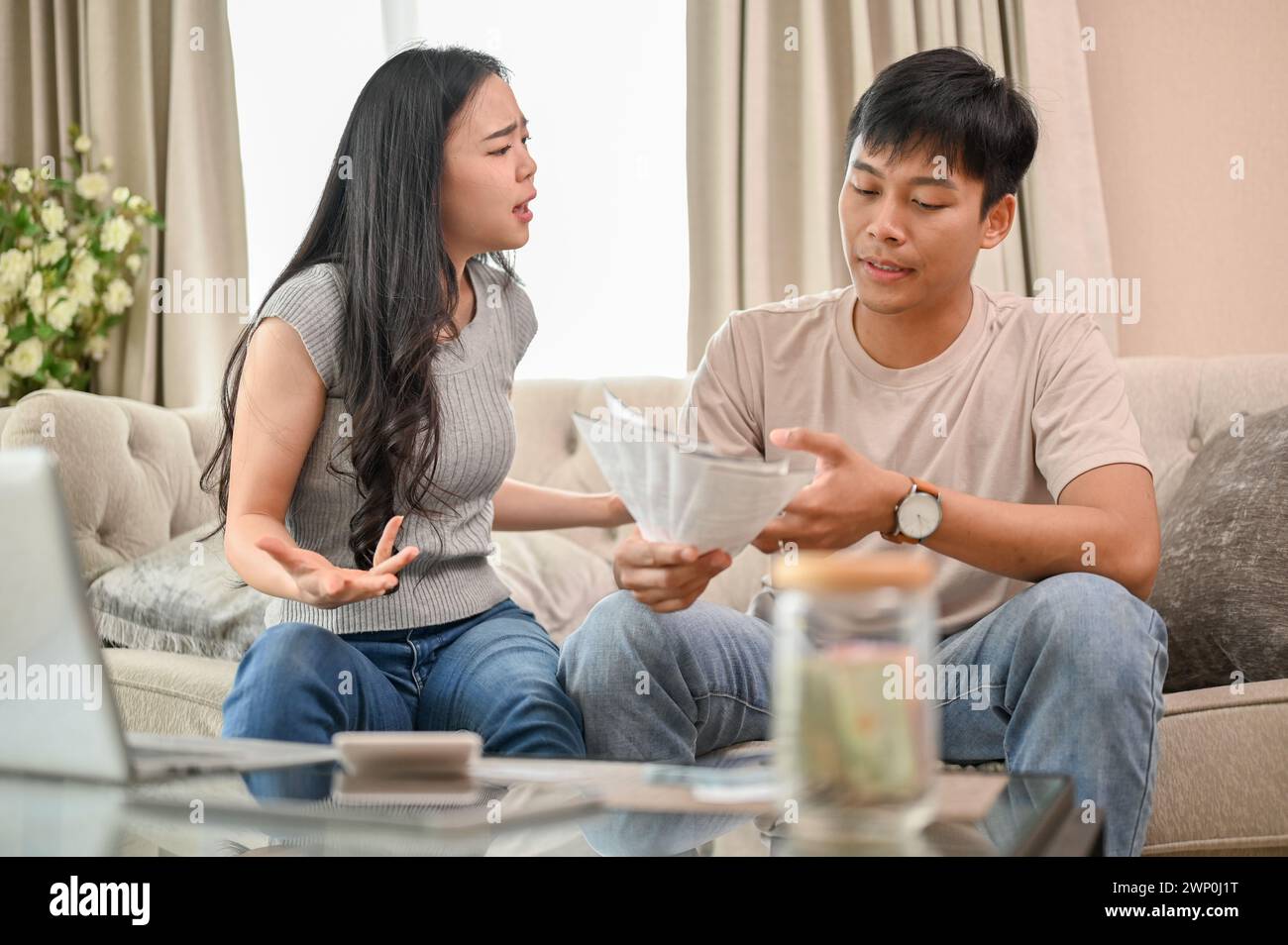 Unhappy, stressed Asian spouses are sitting on a couch, arguing about ...