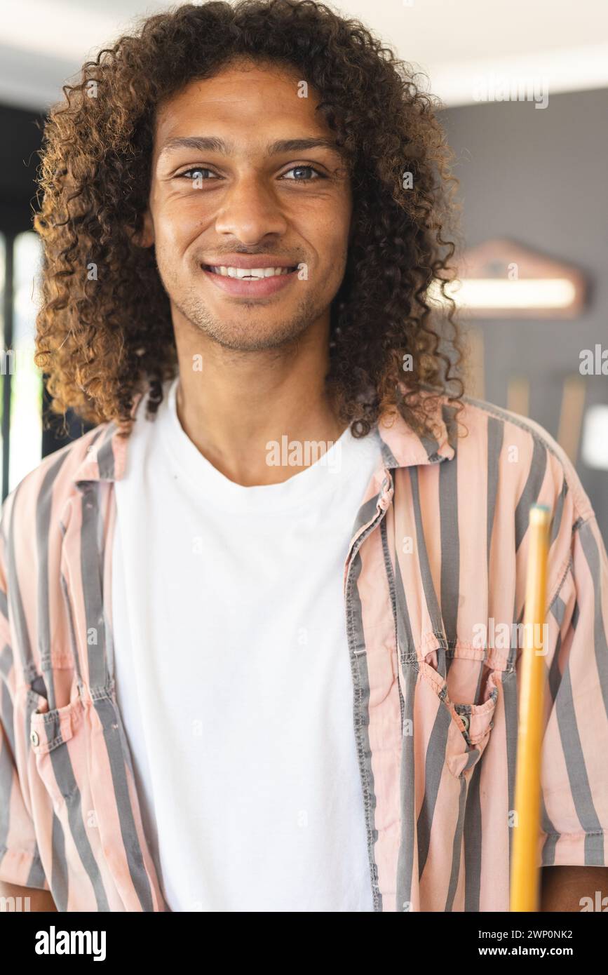 Young biracial man with curly hair smiles warmly, holding a pool cue Stock Photo - Alamy