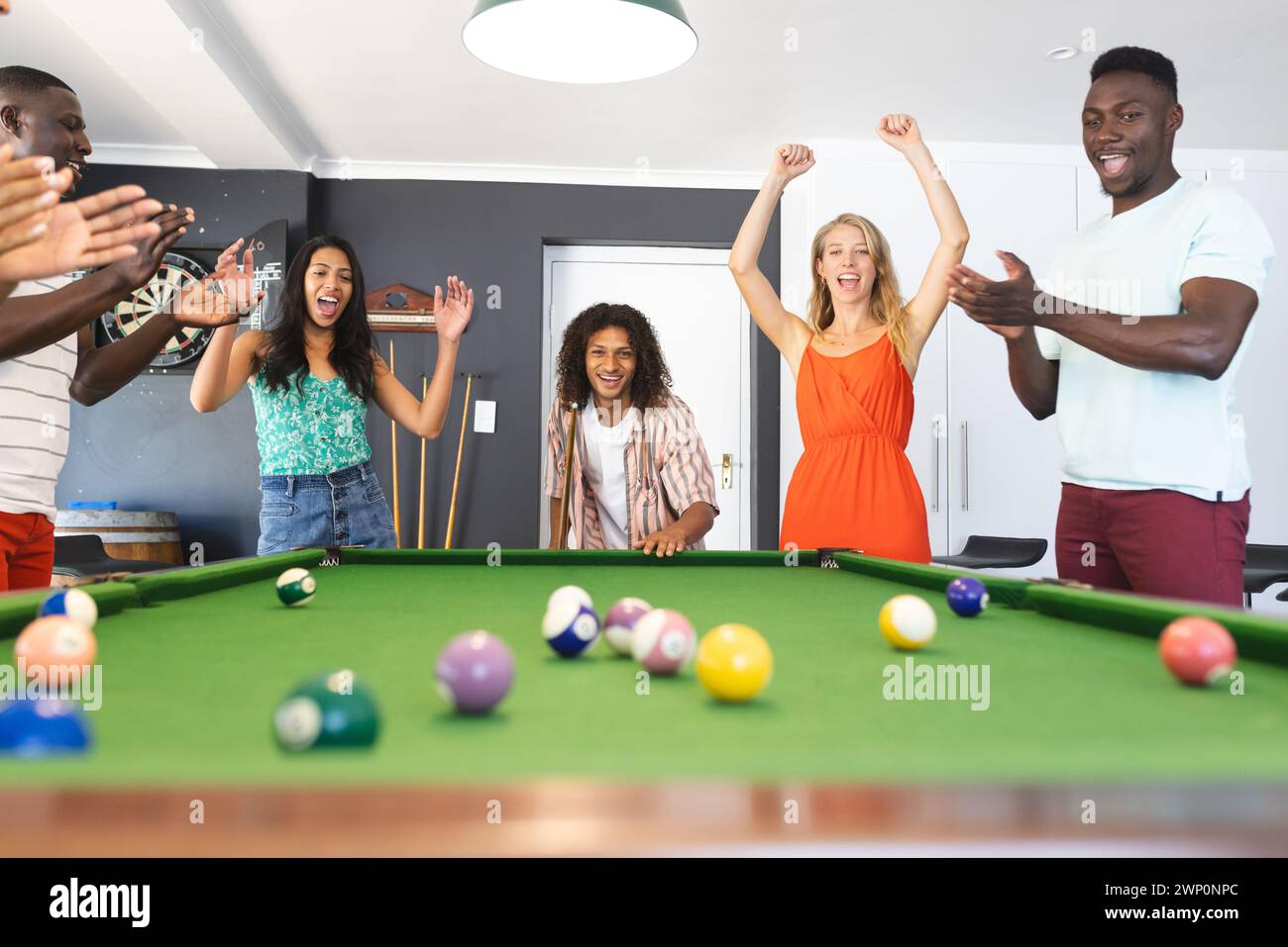 Diverse group of friends celebrates around a pool table, with a young ...