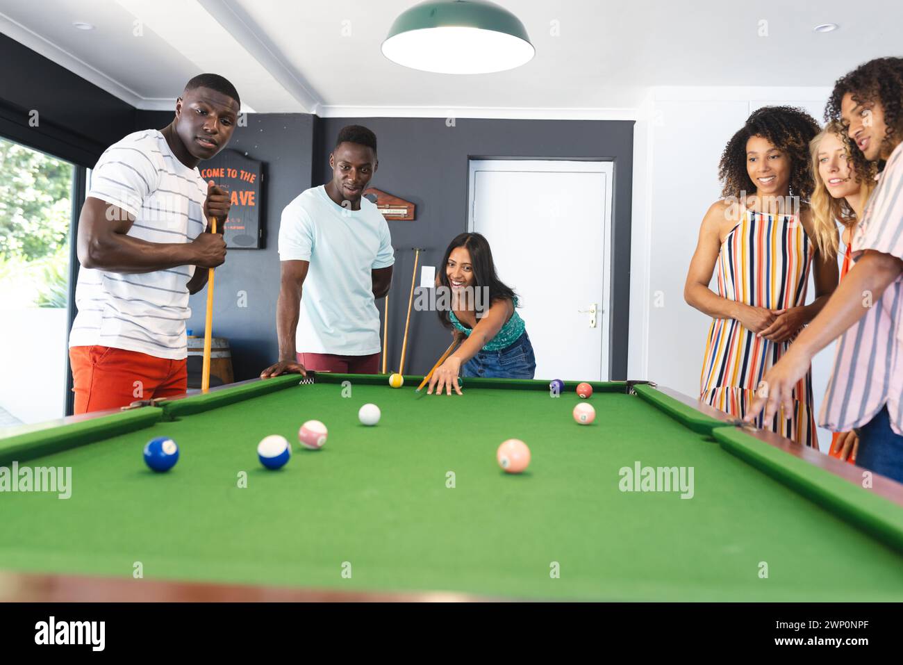 Diverse group of friends enjoy a game of pool, with a young African ...