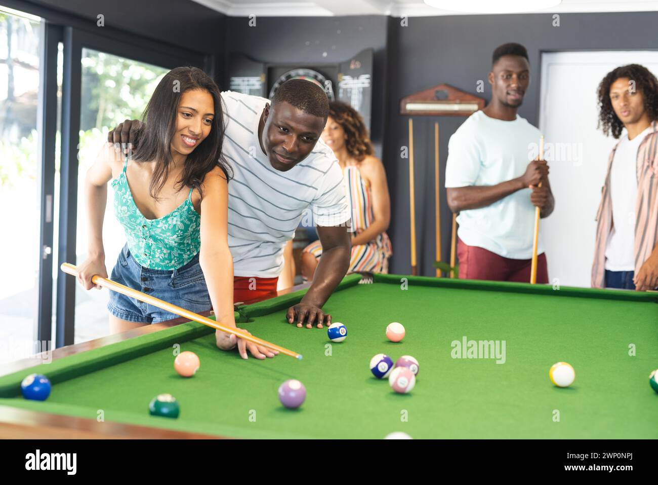 Biracial woman and African American man play pool as another African ...