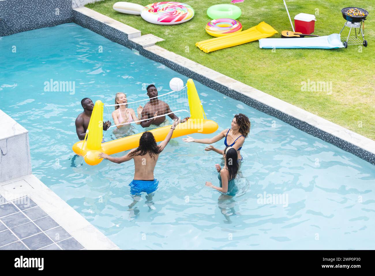 Diverse group of friends enjoy a game of volleyball in a pool ...