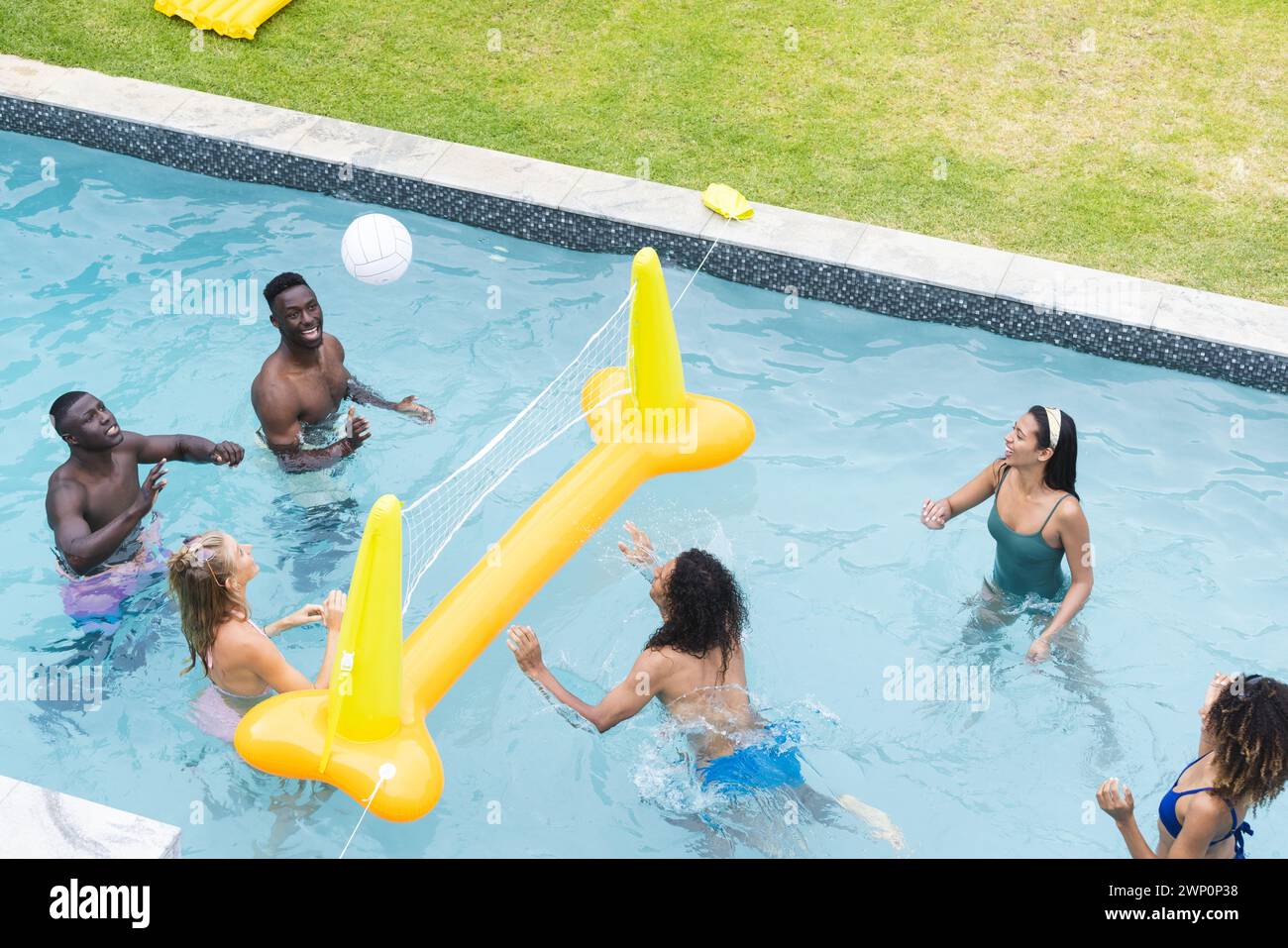 Diverse group of friends enjoy a game of volleyball in a pool, with a ...