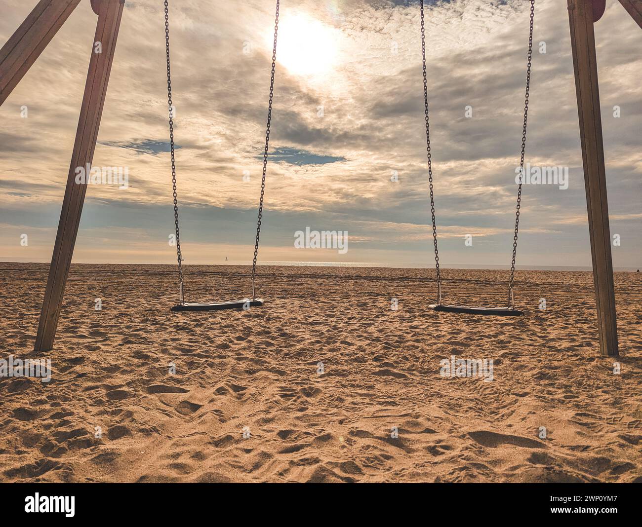 Swings hanging from erected wooden poles on sandy beach with chains in ...