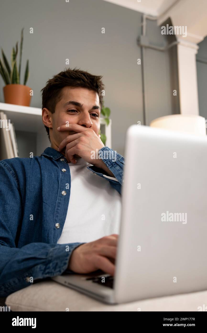 Excited young adult man laughing while using a laptop at home ...