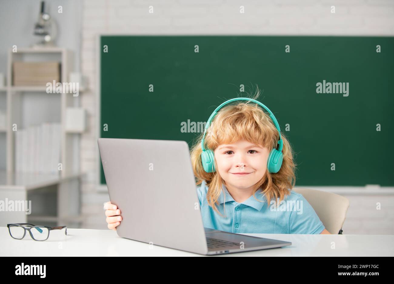 Cute smiling boy wearing headphones, study with laptop in classroom ...