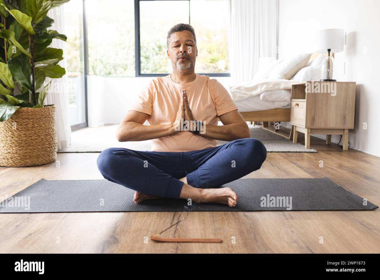 Biracial senior man meditates with hands in prayer position, seated on ...
