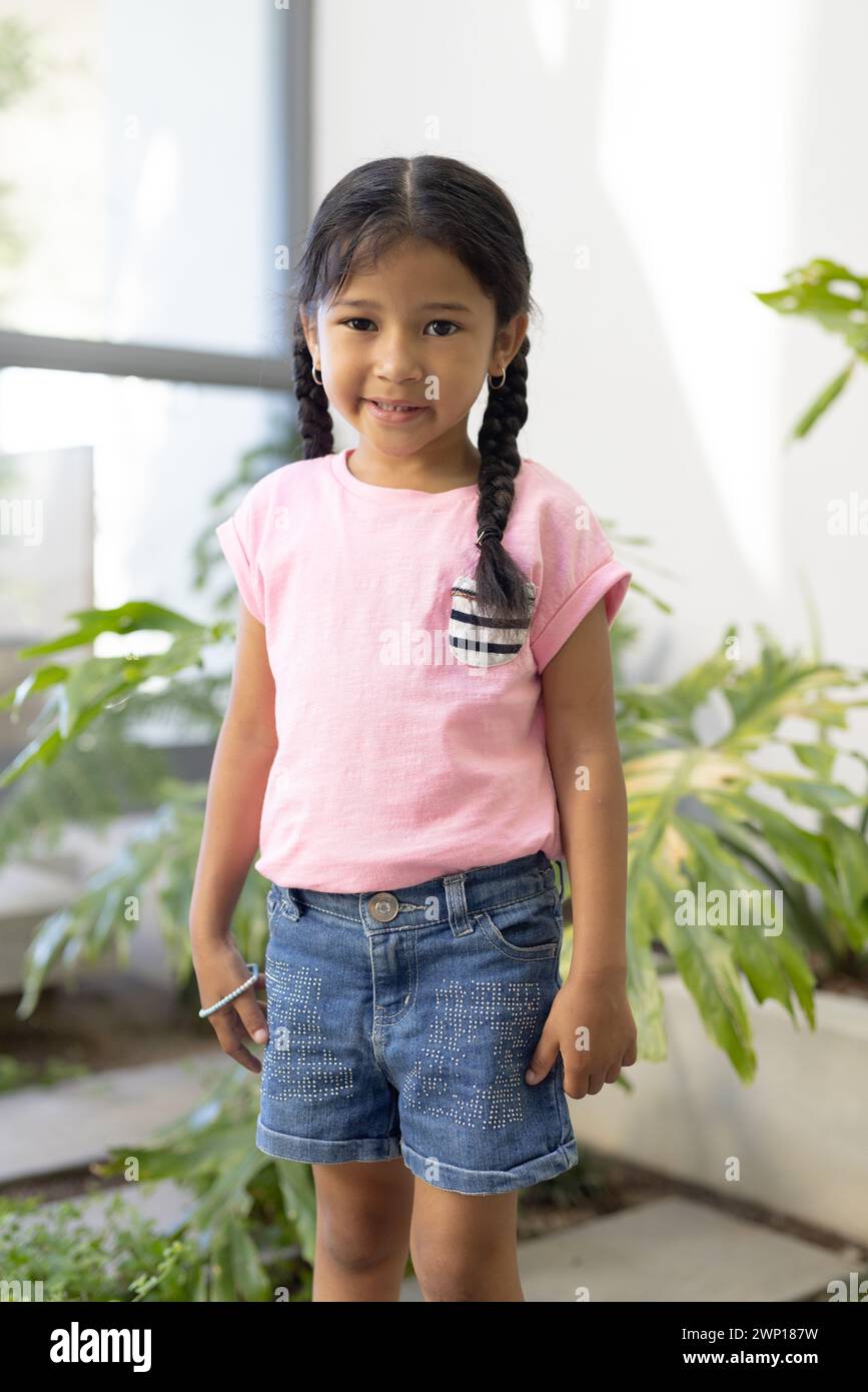 Biracial girl with braided hair stands smiling in a pink shirt and ...
