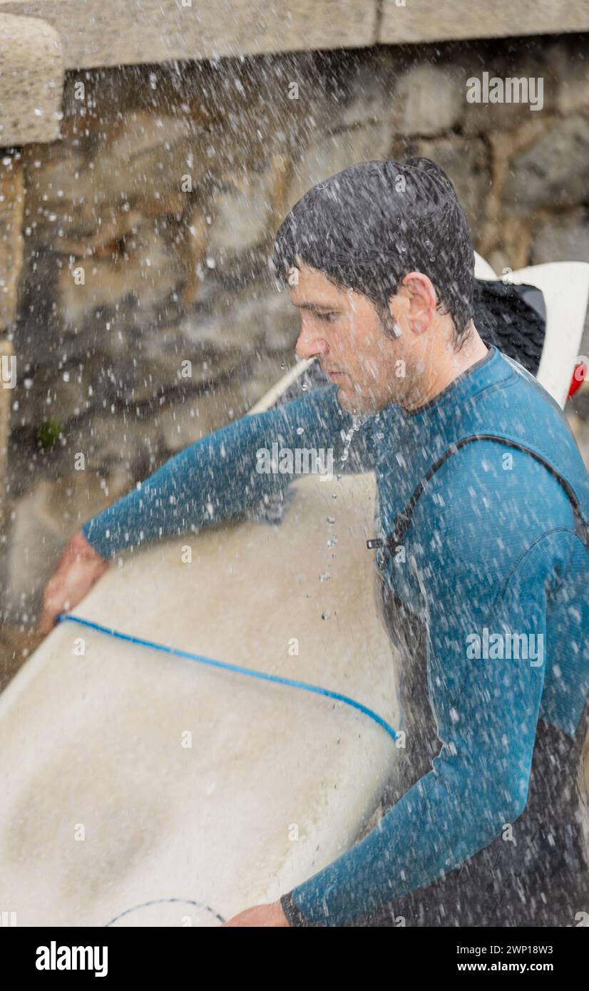 A surfer, holding his board, enjoys the refreshing droplets of an ...