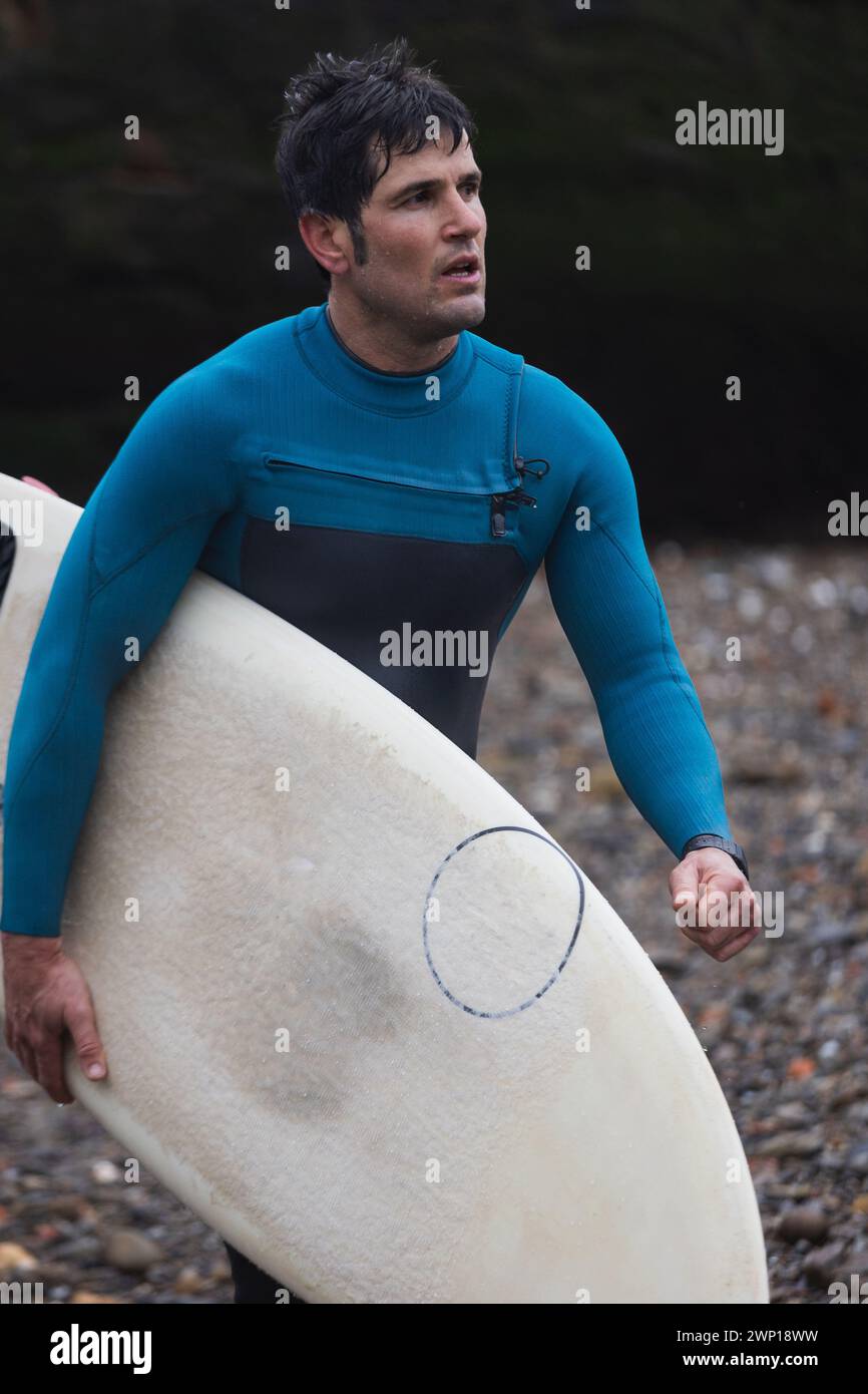 A determined surfer exits the water holding his board, showing signs of ...
