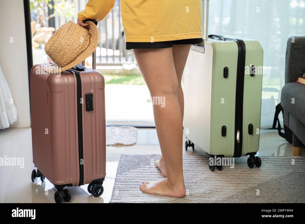 Low section of woman dragging her suitcase, carrying a sunhat and ...