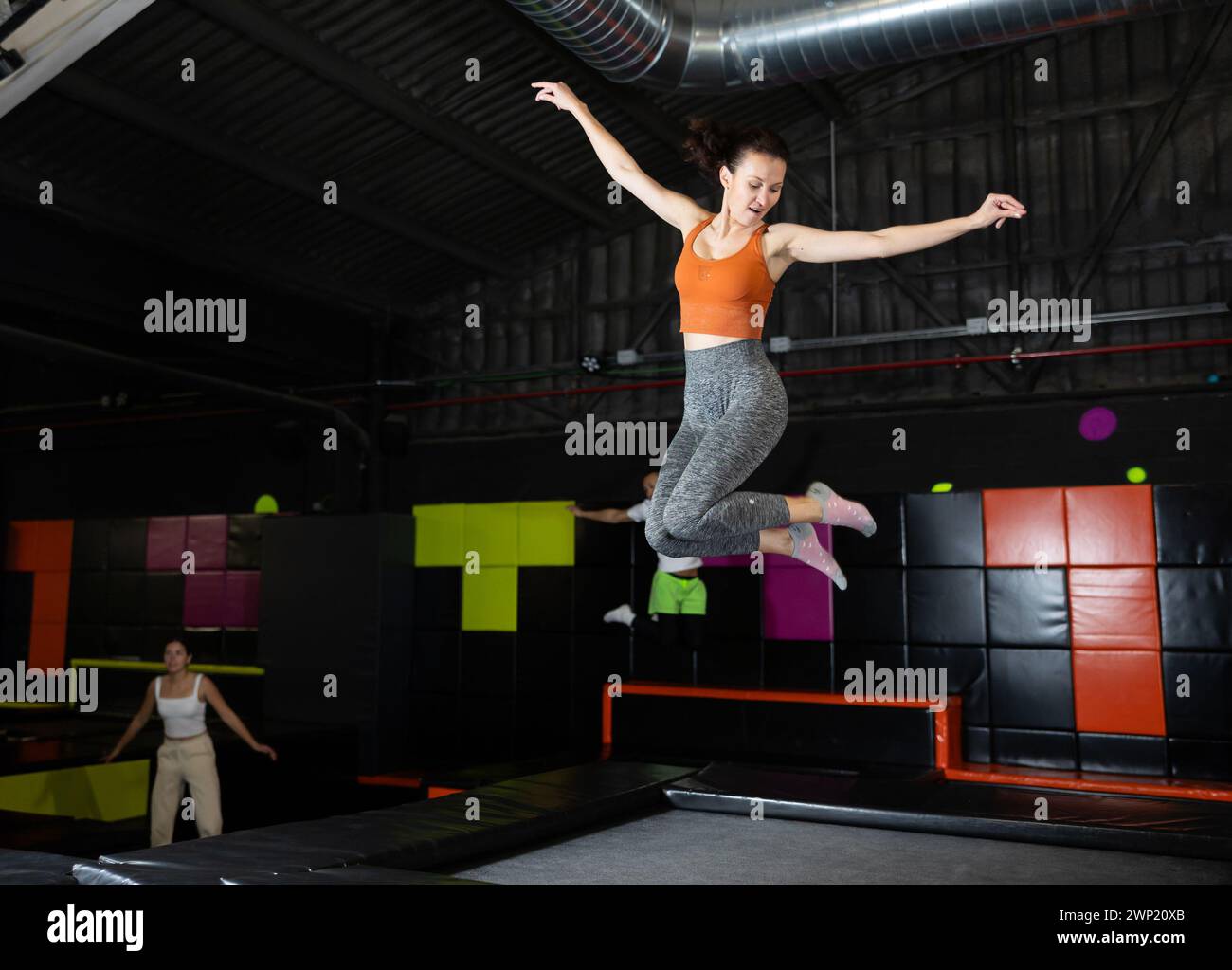 Excited woman enjoying jumping at well-equipped indoor trampoline arena ...