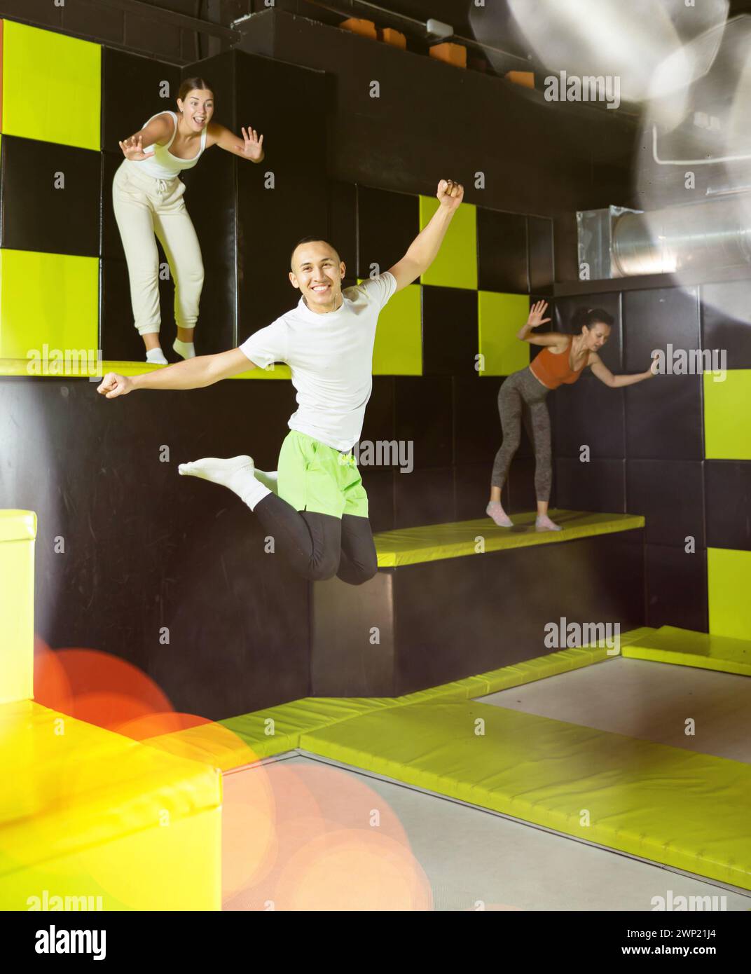 Joyful young man jumping on trampolines in colorful amusement park ...