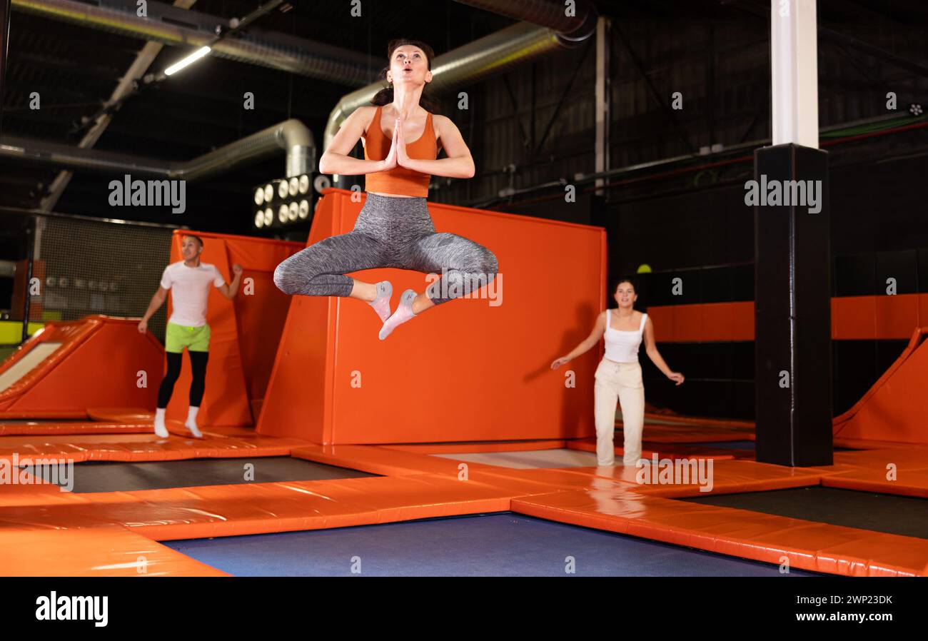 Happy middle aged woman practicing and jumping on trampolines in a sports indoor center, workout ...