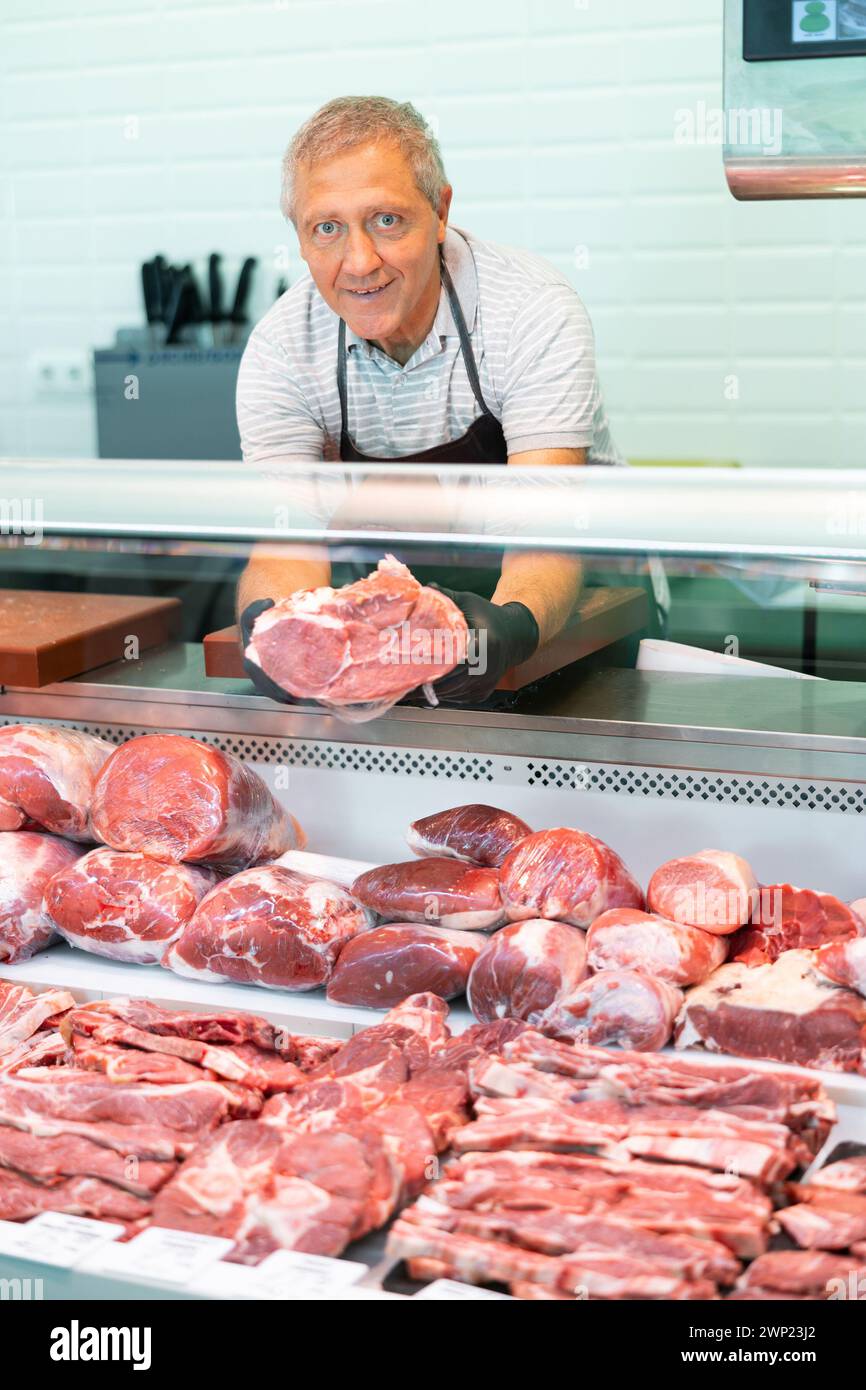 Elderly butcher shop seller laying out fresh beef in display case Stock ...