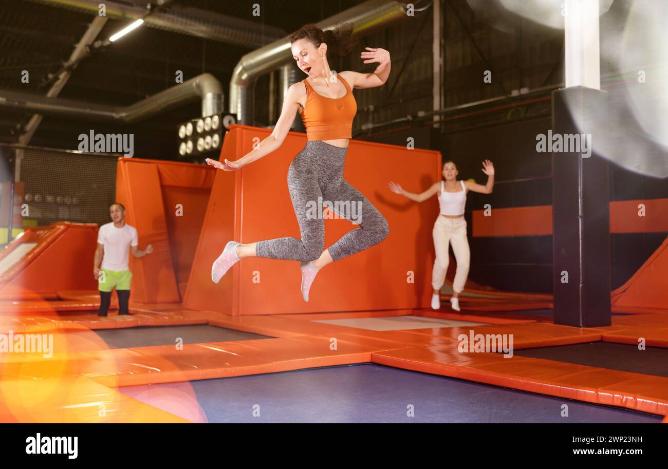 Happy middle aged woman practicing and jumping on trampolines in a sports indoor center, workout ...