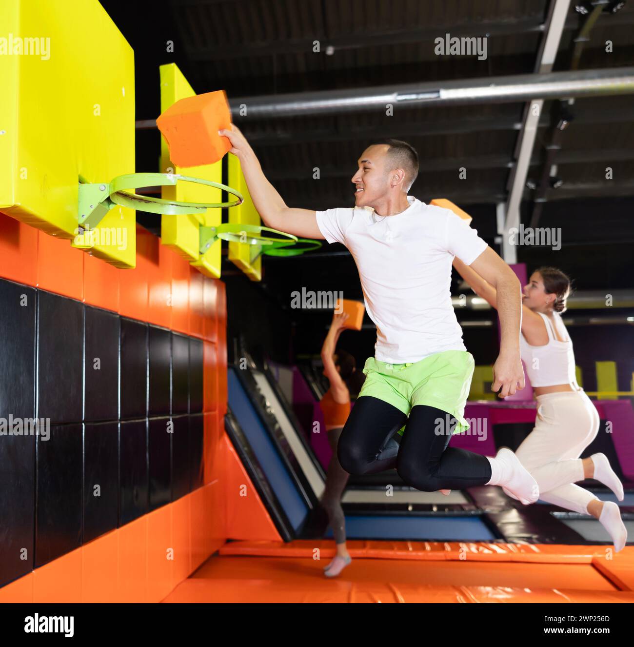 Playful man aiming foam cube at basketball hoop at trampoline park ...