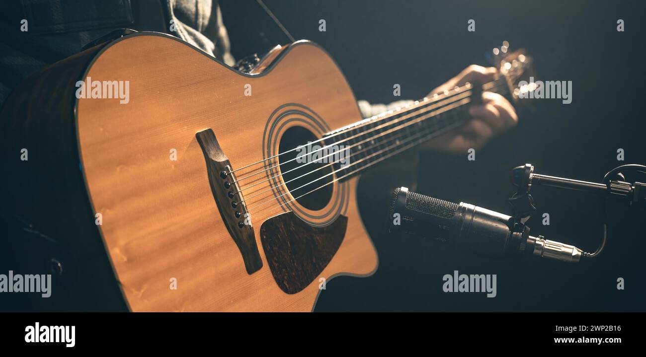 Male musician playing acoustic guitar behind microphone in recording ...