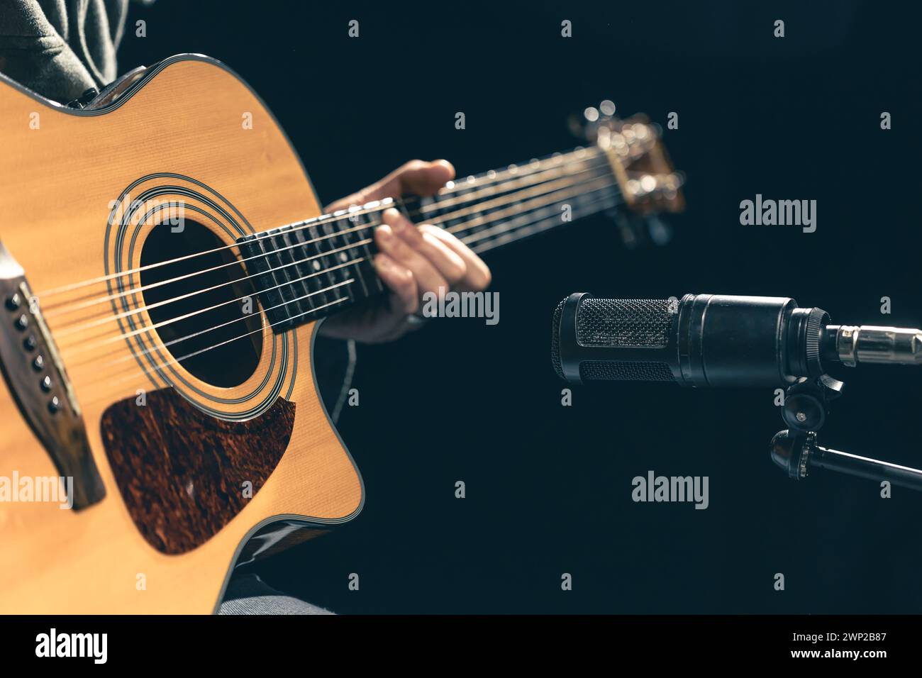Male musician playing acoustic guitar behind microphone in recording ...