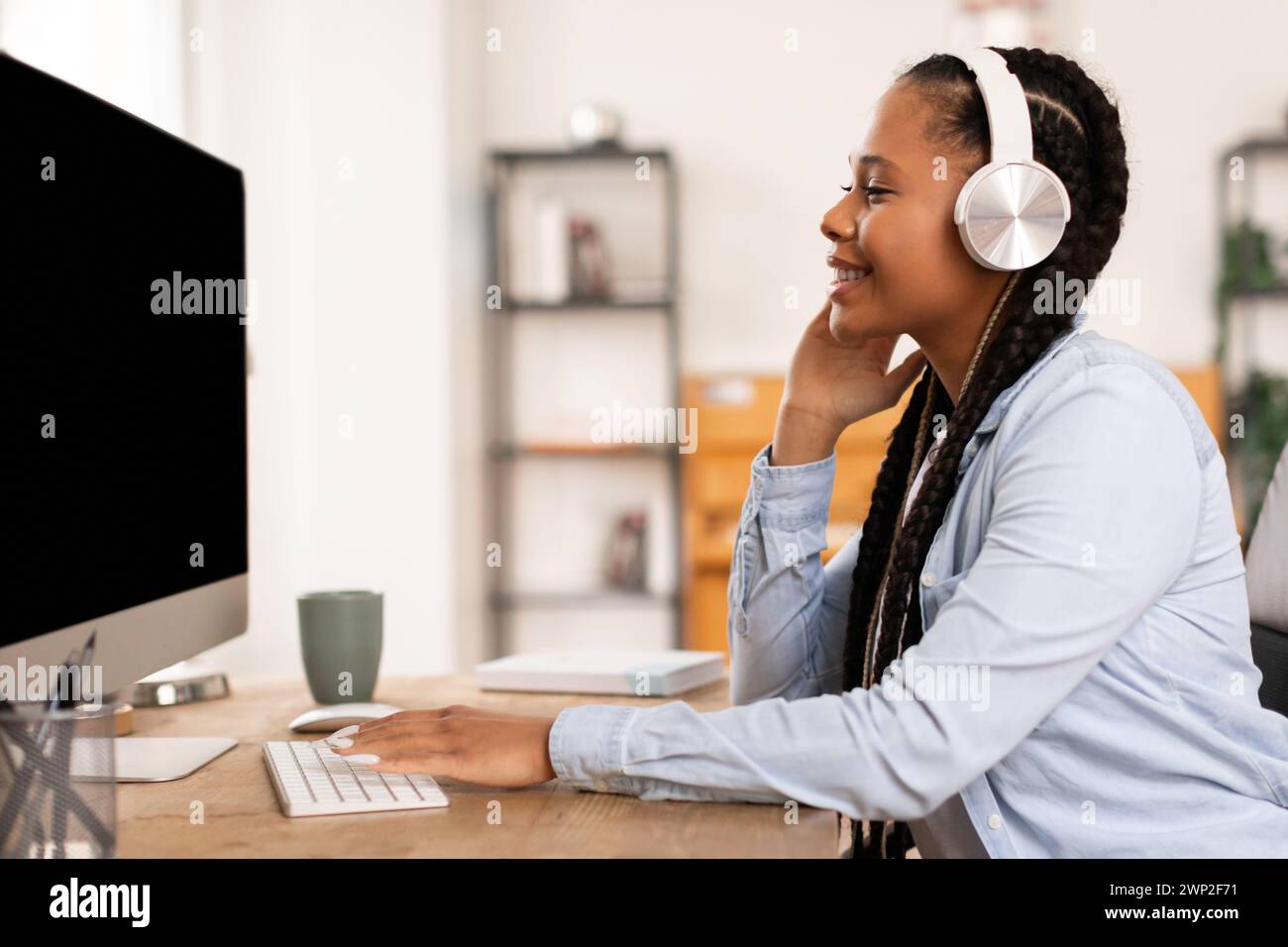 Focused black female teen studying online with headphones and computer ...