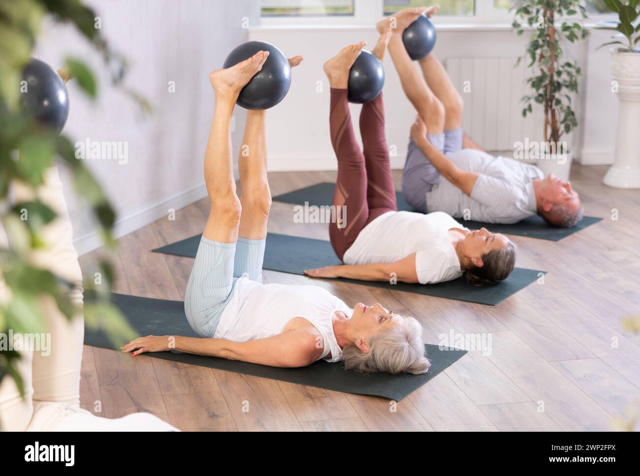 Mature woman doing exercises with pilates ball during group training at ...