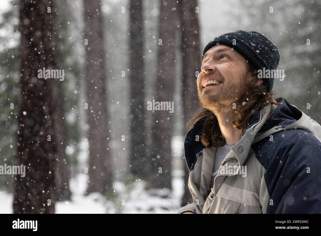 A man wearing a black hat and a blue jacket is smiling as he looks up ...