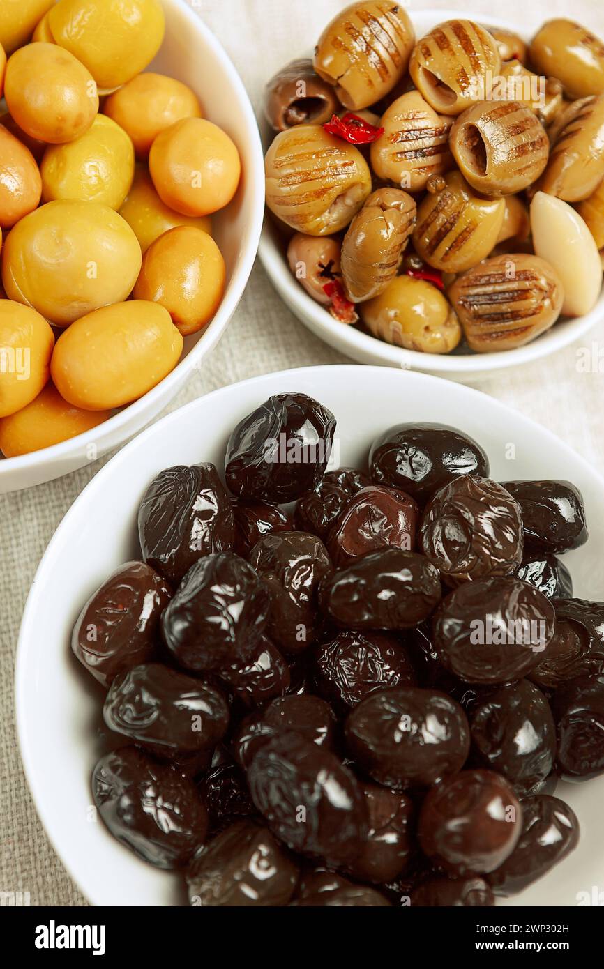 a set of three types of olives in white bowls - whole large green ...