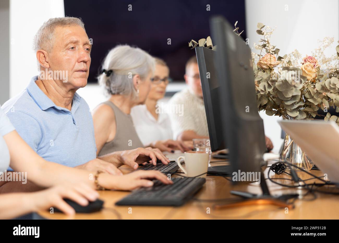 Focus on senior man who is learning to work on computer in group of ...