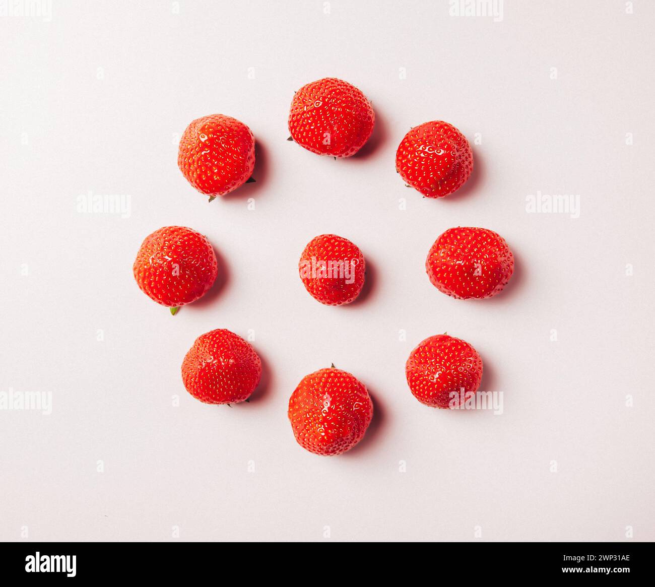 whole ripe strawberries laid out in a circle on a pink background, one ...