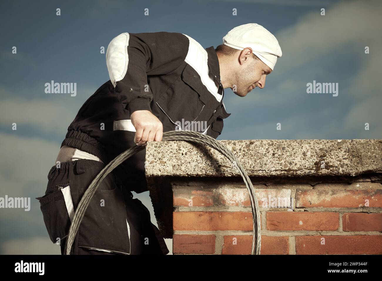 Chimney sweep man in work uniform cleaning brick style chimney on ...