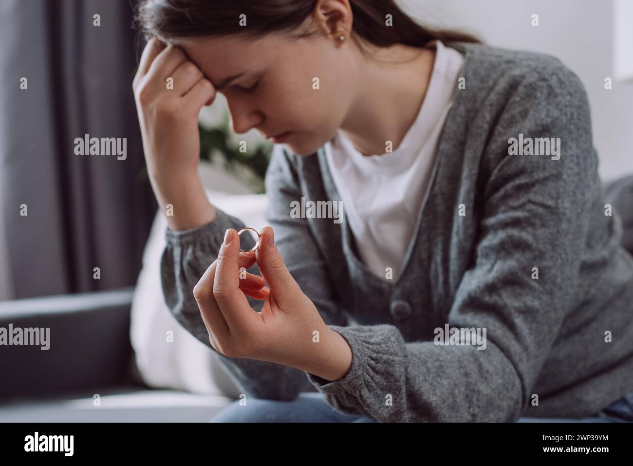 Selective focus of upset worried young woman holding wedding ring think ...