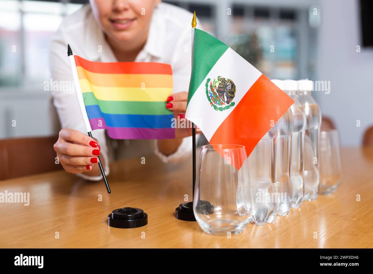 A woman in a white blouse with friendly smile arrangs flags of Mexico ...