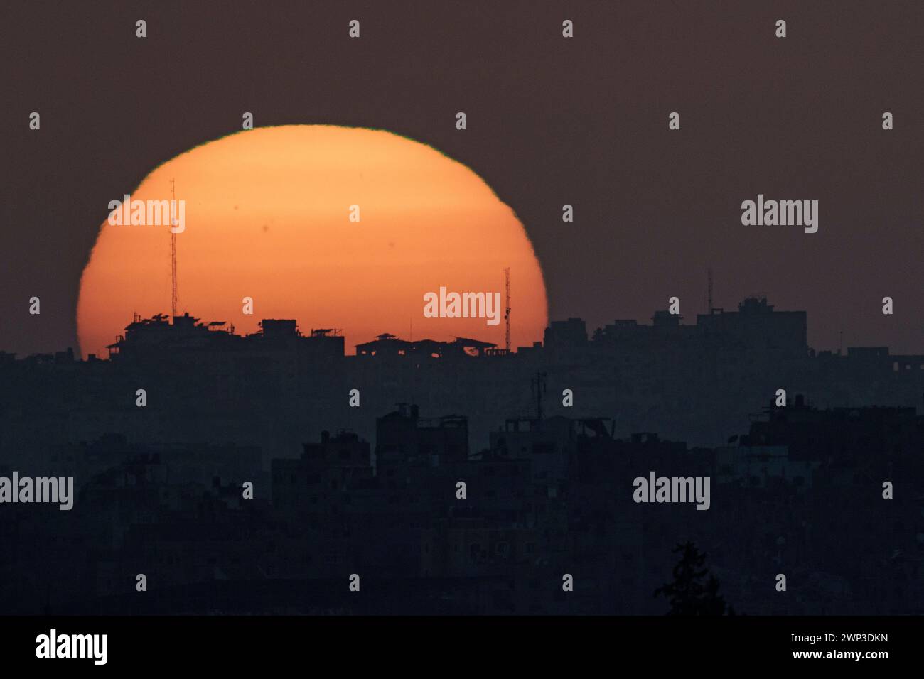 The sun sets behind the buildings in the Gaza Strip as seen from ...