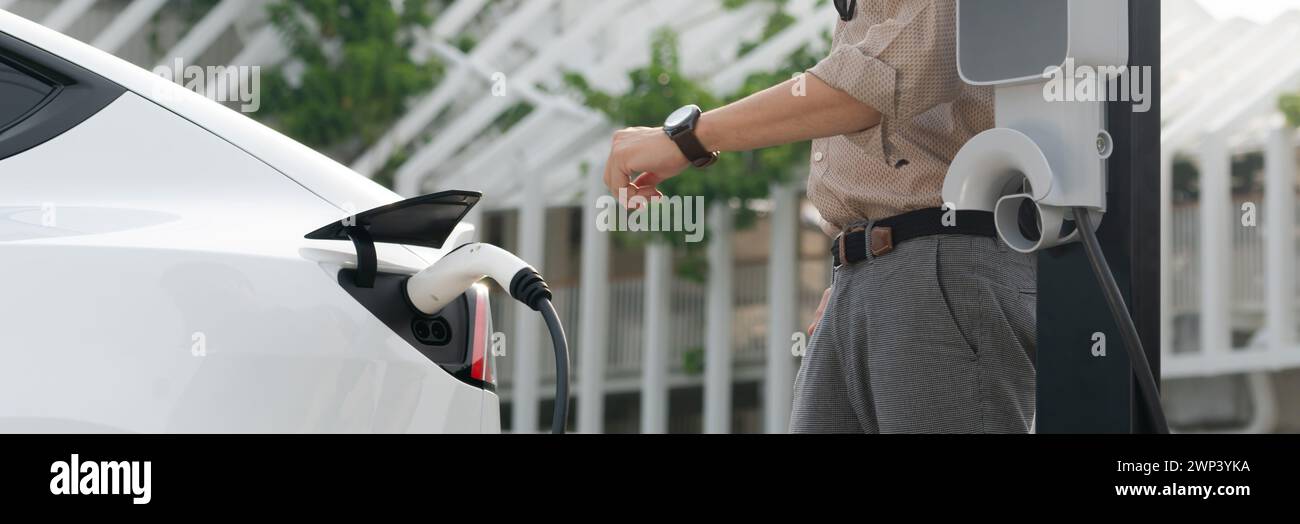 Young man checking time on smartwatch while EV charger to recharging ...