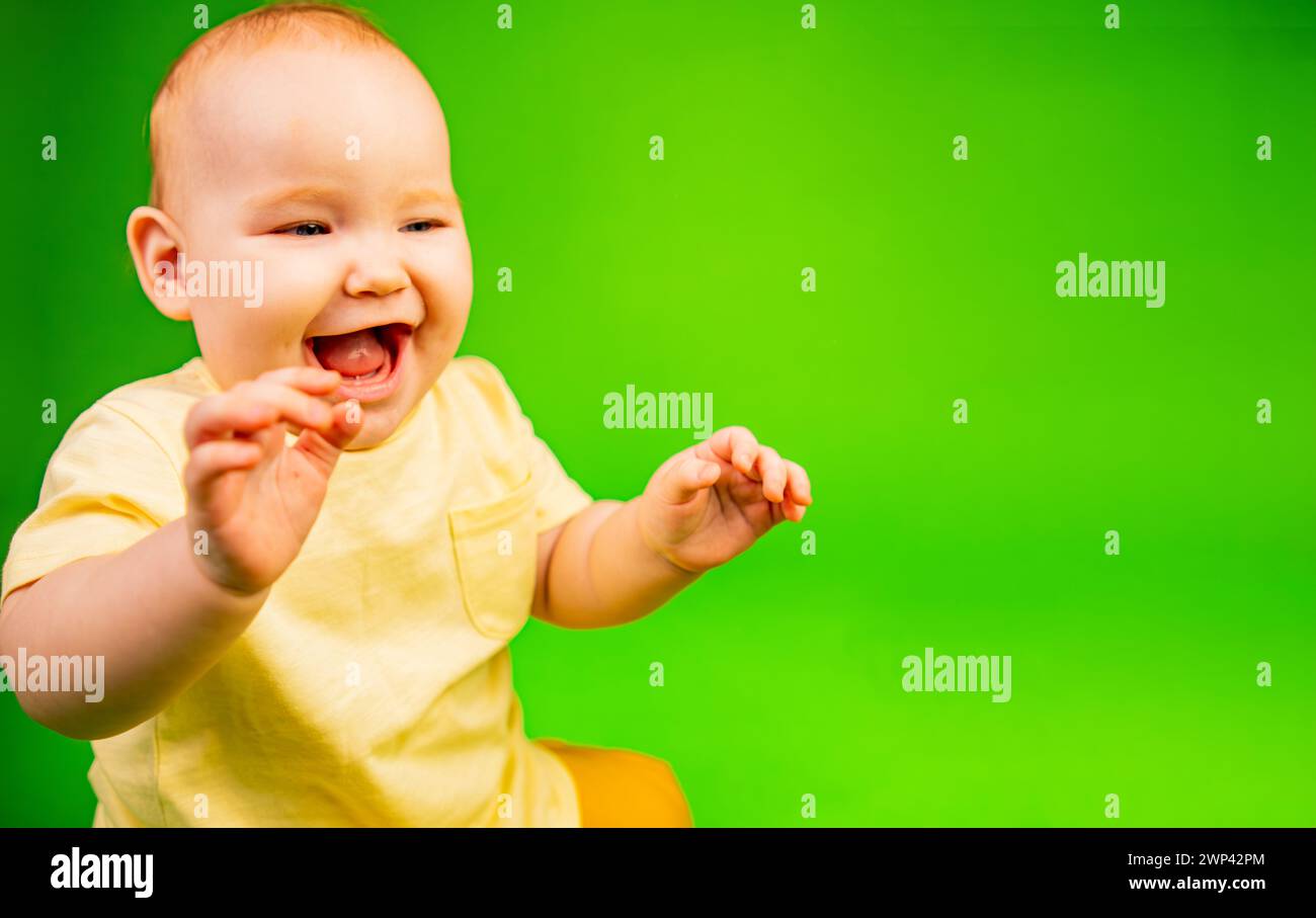 A cheerful baby laughs with hands outstretched against a bright green ...